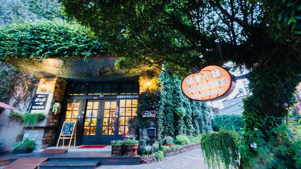 Restaurante com entrada escura, rodeado por vegetação exuberante e uma placa pendurada.