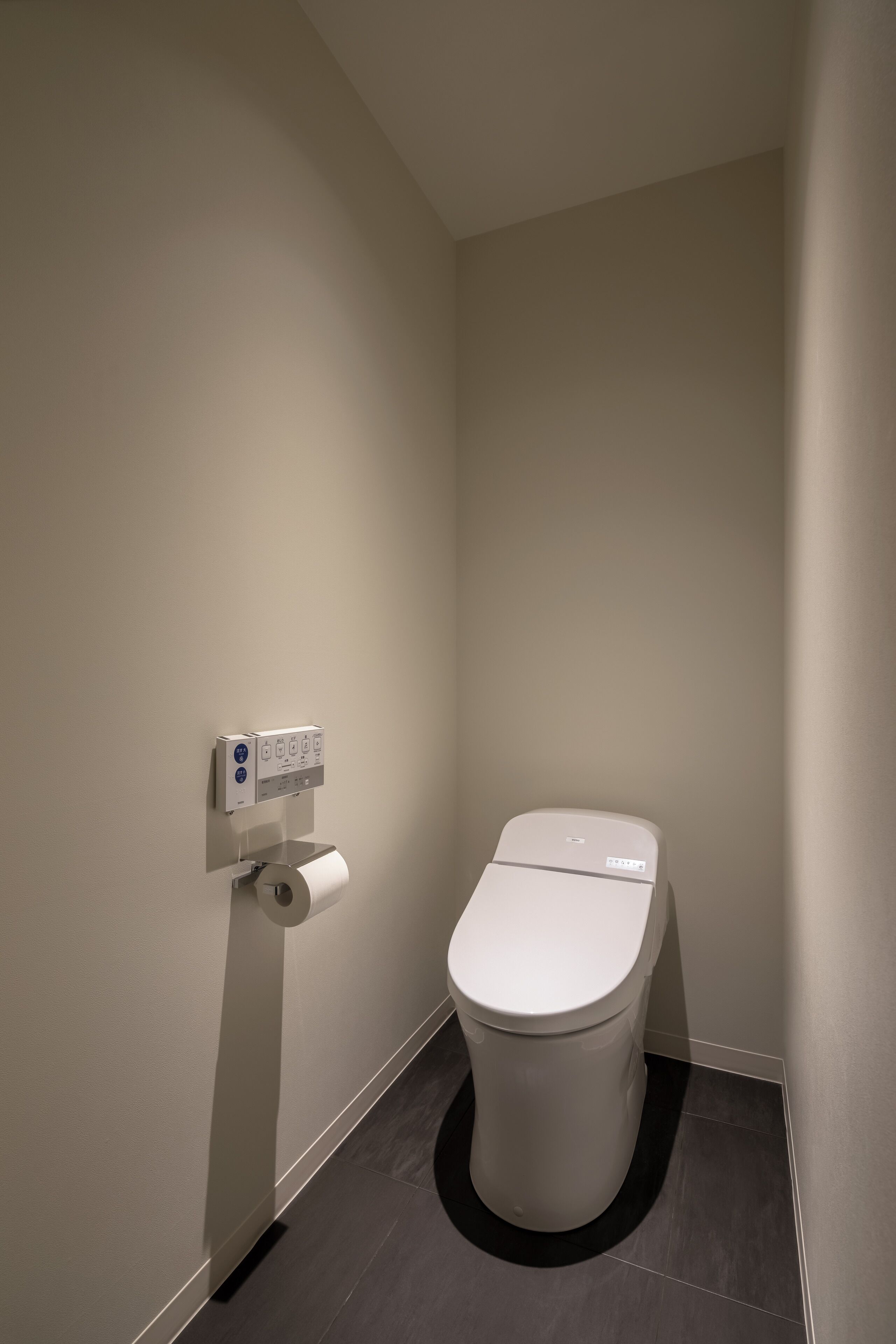Casa de banho pequena e moderna com sanita, dispensador de papel higiénico na parede e tapete preto.