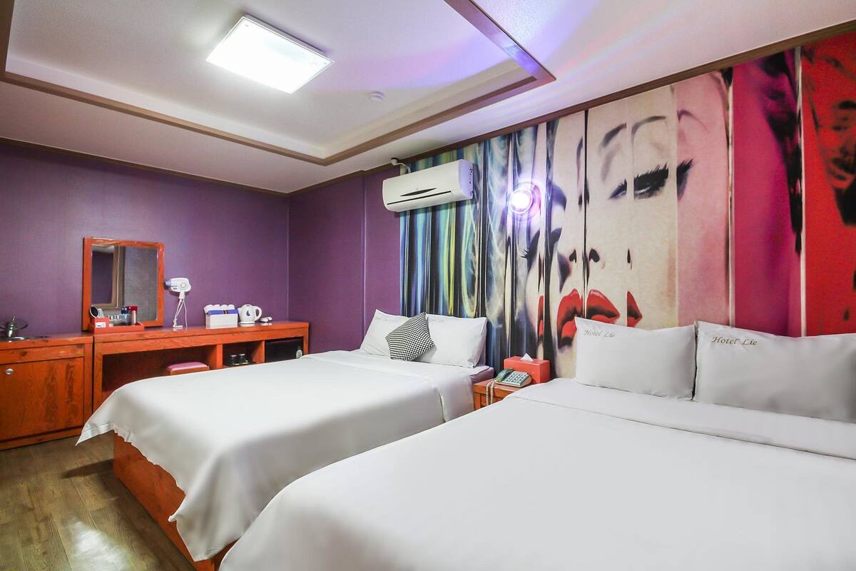Quarto de hotel com duas camas, uma escrivaninha com espelho, telefone e ar condicionado.