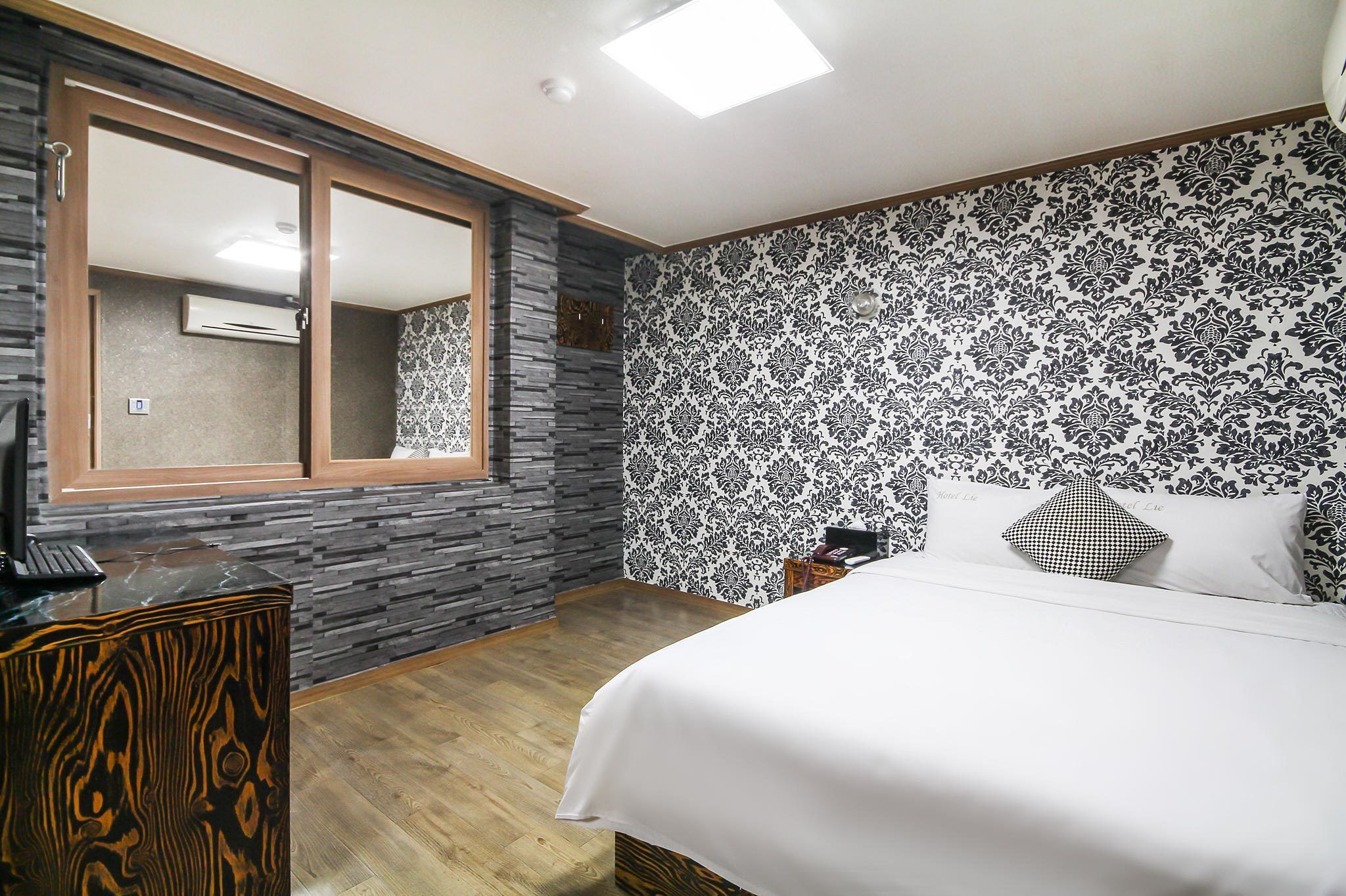 Quarto com cama, escrivaninha, espelho e papel de parede estampado.