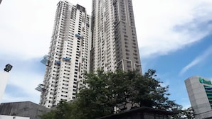 Dois edifícios altos com vários andares, cercados por árvores e um céu limpo.