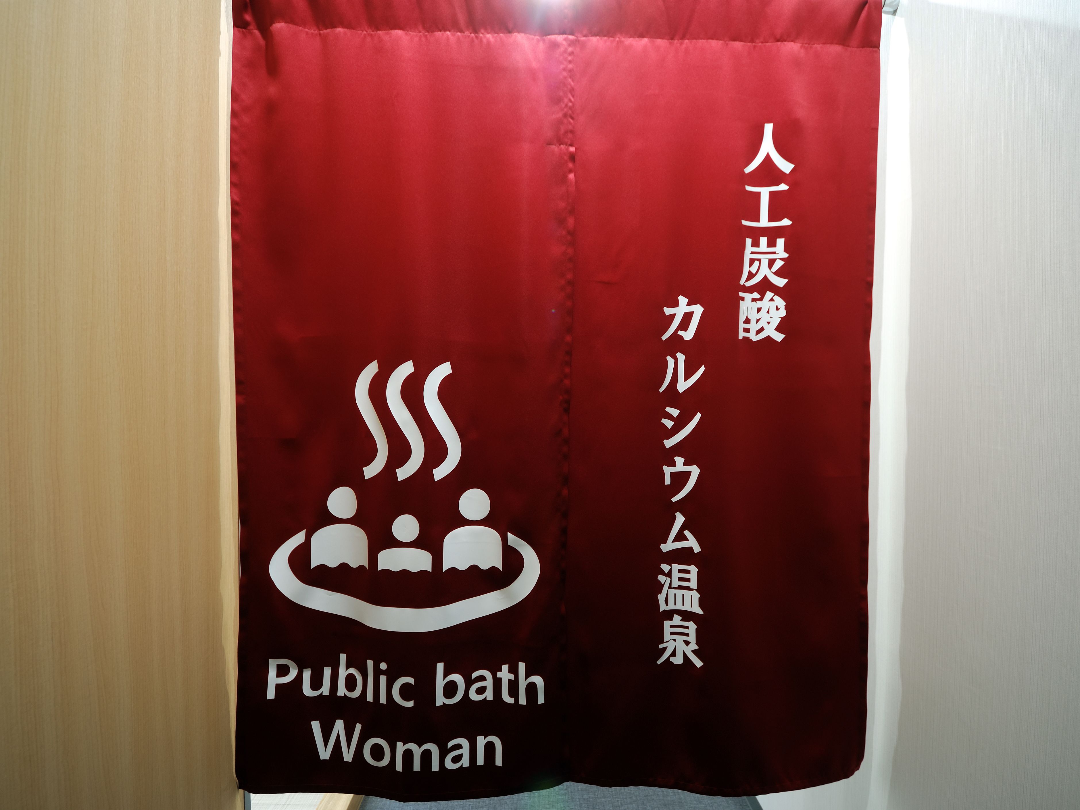 Tapete de banho vermelho com texto em japonês e um ícone de banho público.