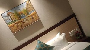 Quarto de hotel com uma cama, um arranjo floral em formato de coração e um quadro de uma cena urbana na parede.