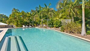 Piscina retangular com águas cristalinas azuis, cercada por vegetação exuberante e palmeiras.
