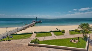 Uma praia com calçada pavimentada, um cais e barcos na água.