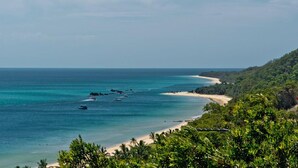 Paisagem costeira com praia, águas azul-claras e vegetação densa.