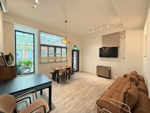 Uma sala de estar moderna com sofá, mesa de jantar, cadeiras e televisão fixada na parede.