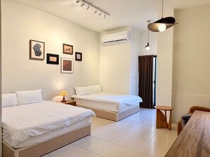 Quarto de hotel com duas camas, uma mesa pequena, uma luminária e ar condicionado fixado na parede.