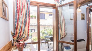 Um quarto com uma mesa de madeira, um vaso com flores secas e uma janela com cortinas.