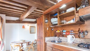 Uma cozinha rústica com armários de madeira, uma pia e um fogão. Há uma mesa de jantar com cadeiras e um lustre.