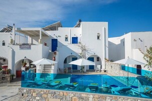 Um edifício branco com área de piscina, portas azuis e espaço para sentar ao ar livre.