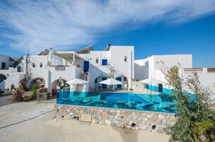 Um edifício branco com piscina e guarda-sóis azuis.