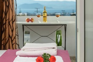 Quarto com cama, mesa com toalhas e uma garrafa, e vista para o mar.