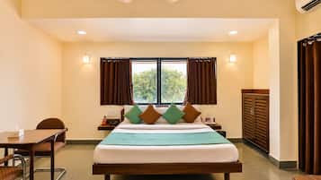 Quarto de hotel com cama, mesa de cabeceira, cadeira e janela com cortinas.