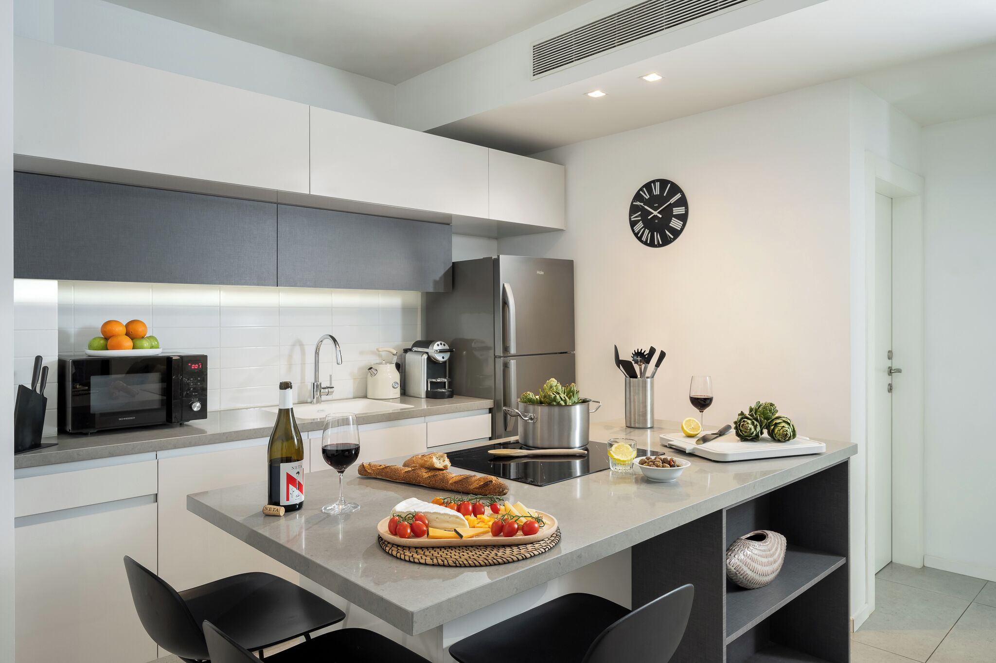 Uma cozinha moderna com uma ilha central, eletrodomésticos de aço inoxidável e um relógio na parede.