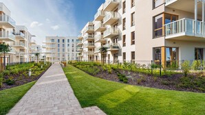 Um complexo de apartamentos moderno com um caminho central, varandas e um gramado bem cuidado.