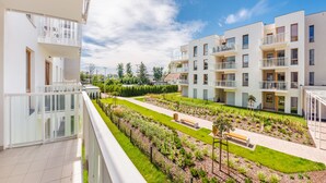 Um complexo de apartamentos moderno com varandas, um pátio central com um caminho e áreas verdes ao redor.