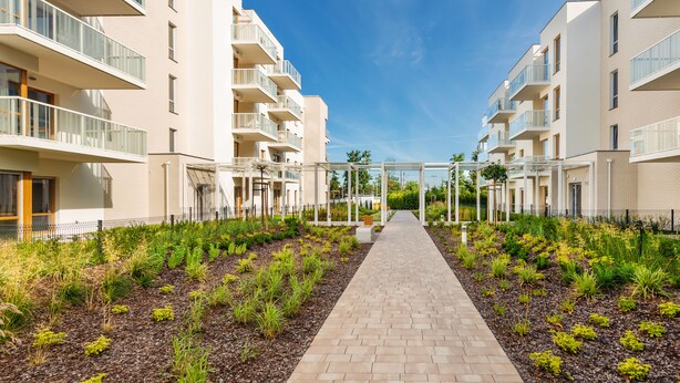 Um edifício de apartamentos moderno com um caminho central, varandas e área de jardim.