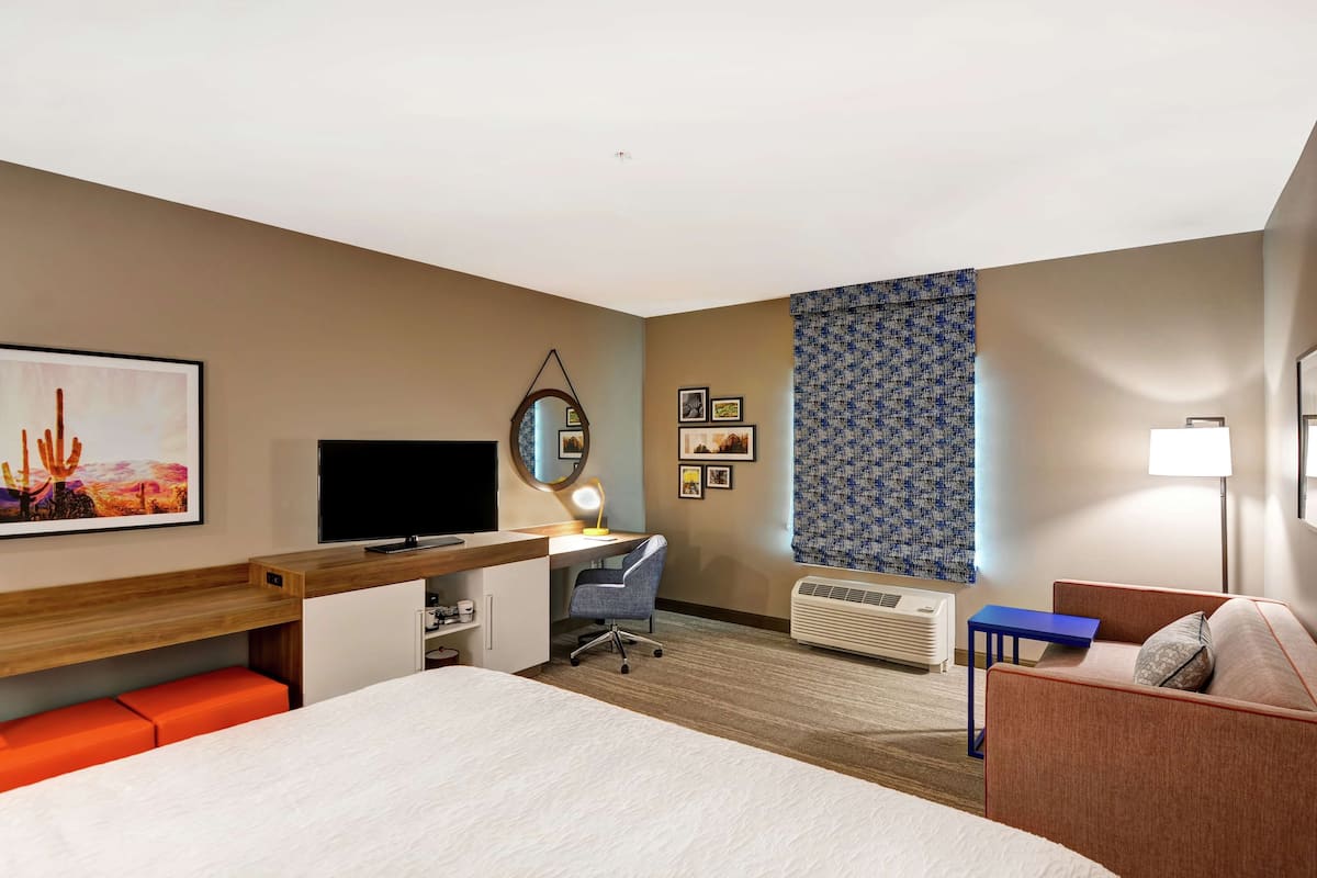 Quarto de hotel com cama, escrivaninha, cadeira, televisão e uma pequena mesa.