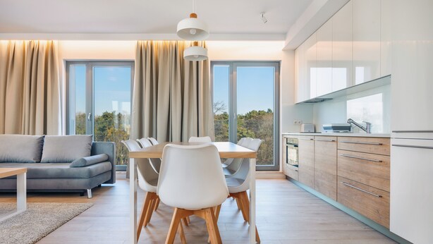 Uma sala de estar moderna com sofá, mesa de jantar e cadeiras. Há uma área de cozinha com armários e uma janela.