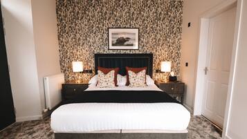 Cama bem arrumada com cabeceira escura, duas luminárias de cabeceira e um quadro emoldurado acima da cama.