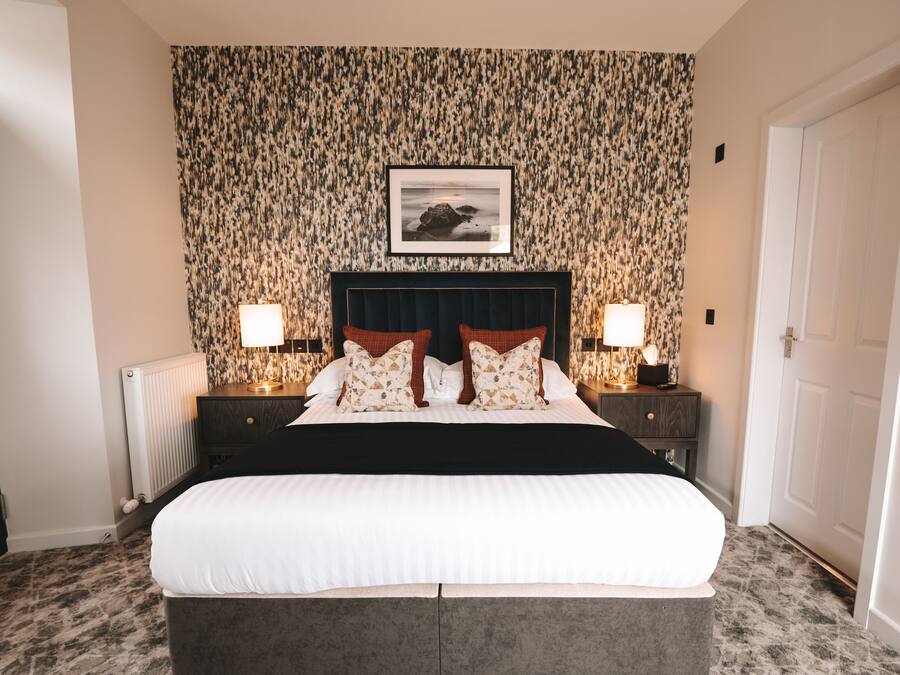 Cama bem arrumada com cabeceira escura, duas luminárias de cabeceira e um quadro emoldurado acima da cama.