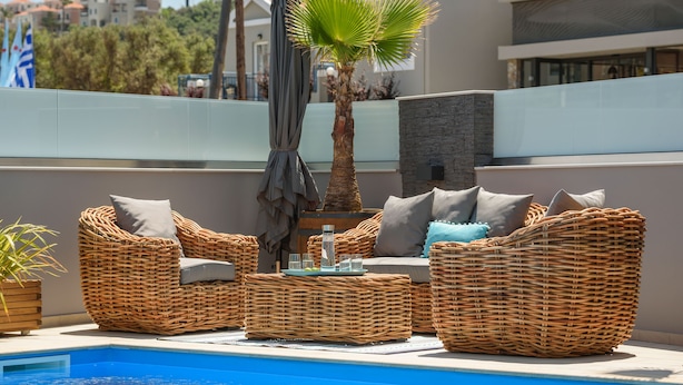 Área de piscina com mobiliário de vime, uma palmeira e vista para edifícios ao fundo.