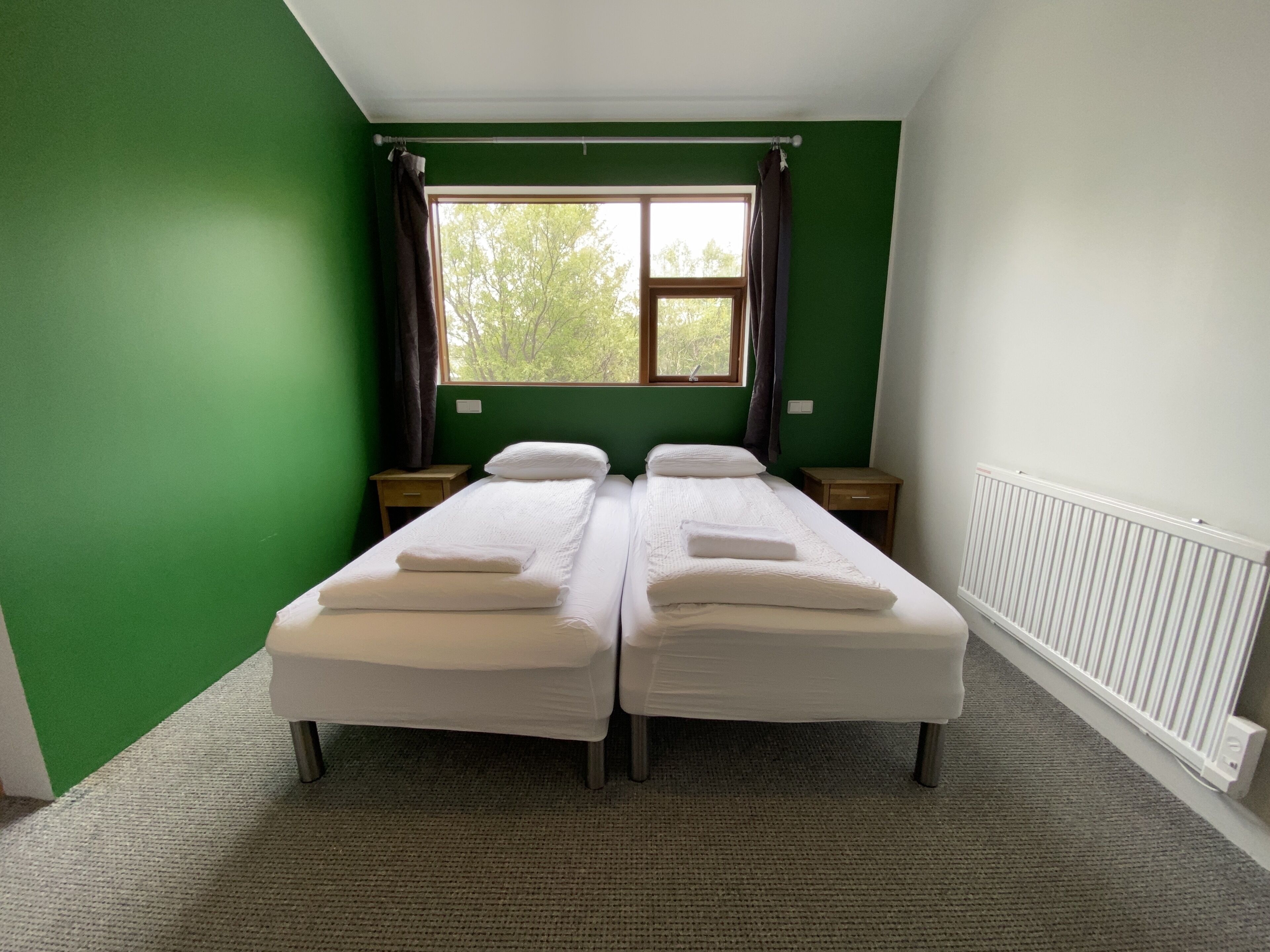 Quarto com duas camas de solteiro, janela com cortinas, radiador e paredes verdes.
