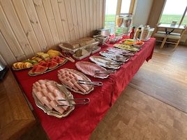 Uma mesa de buffet com diversos alimentos e acompanhamentos, em um espaço com paredes de madeira e vista para o exterior.