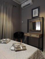 Quarto de hotel com cama, escrivaninha com espelho, cadeira e ar-condicionado fixado na parede.