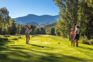 Um campo de golfe com montanhas ao fundo, árvores e céu claro.
