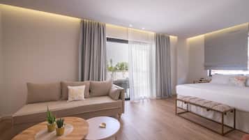 Quarto de hotel moderno com sofá, cama, mesa pequena e um banco. Há uma janela com cortinas e vista para áreas verdes.