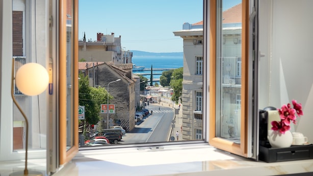 Vista da janela para a rua, com edifícios e céu claro.