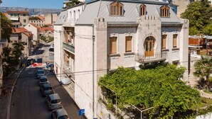 Um edifício com uma entrada em arco notável, uma varanda com guarda-corpo de metal e uma rua com carros estacionados.