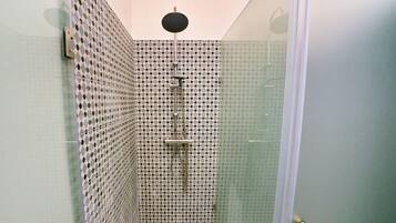 Chuveiro com padrão geométrico de azulejos, chuveiro manual e porta de vidro.