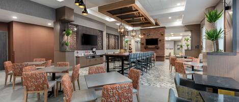 Um restaurante moderno com várias áreas de refeição, incluindo um bar central e diversas mesas com cadeiras estampadas.