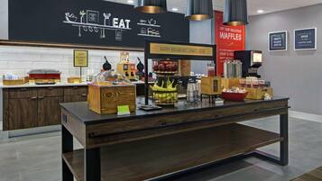 Espaço de buffet de café da manhã com uma placa que diz 'HAPPY BREAKFAST STARTS HERE' e outra placa anunciando waffles.