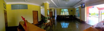 Um hall amplo com piso lustroso, um balcão de recepção e uma escadaria para os andares superiores.