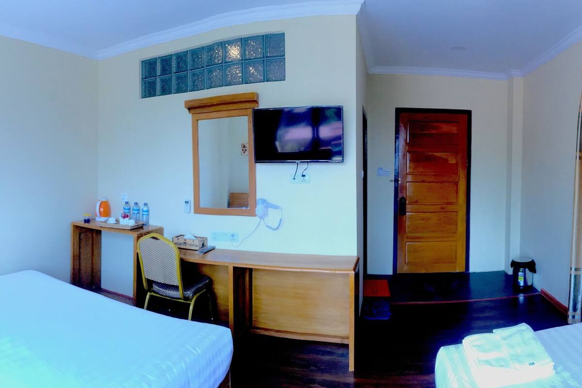 Quarto de hotel com duas camas, uma escrivaninha, uma cadeira, uma televisão e um espelho.