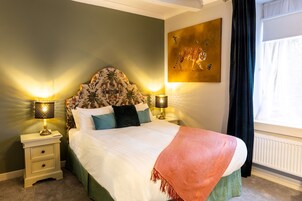 Cama bem arrumada com cabeceira floral, duas luminárias de apoio e um quadro grande de um tigre na parede.