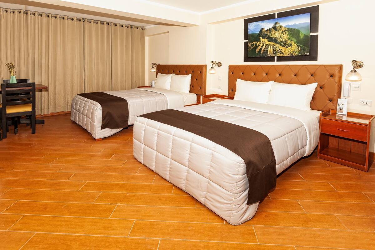 Quarto de hotel com duas camas, uma escrivaninha e uma cadeira.