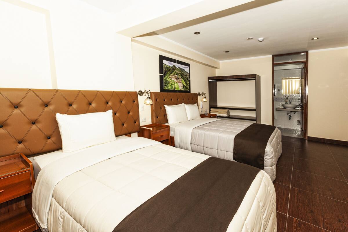 Quarto de hotel com duas camas, um espelho grande, banheiro com pia e um quadro na parede.