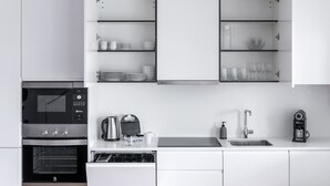 Uma cozinha moderna com armários brancos, forno embutido, cafeteira e pia.