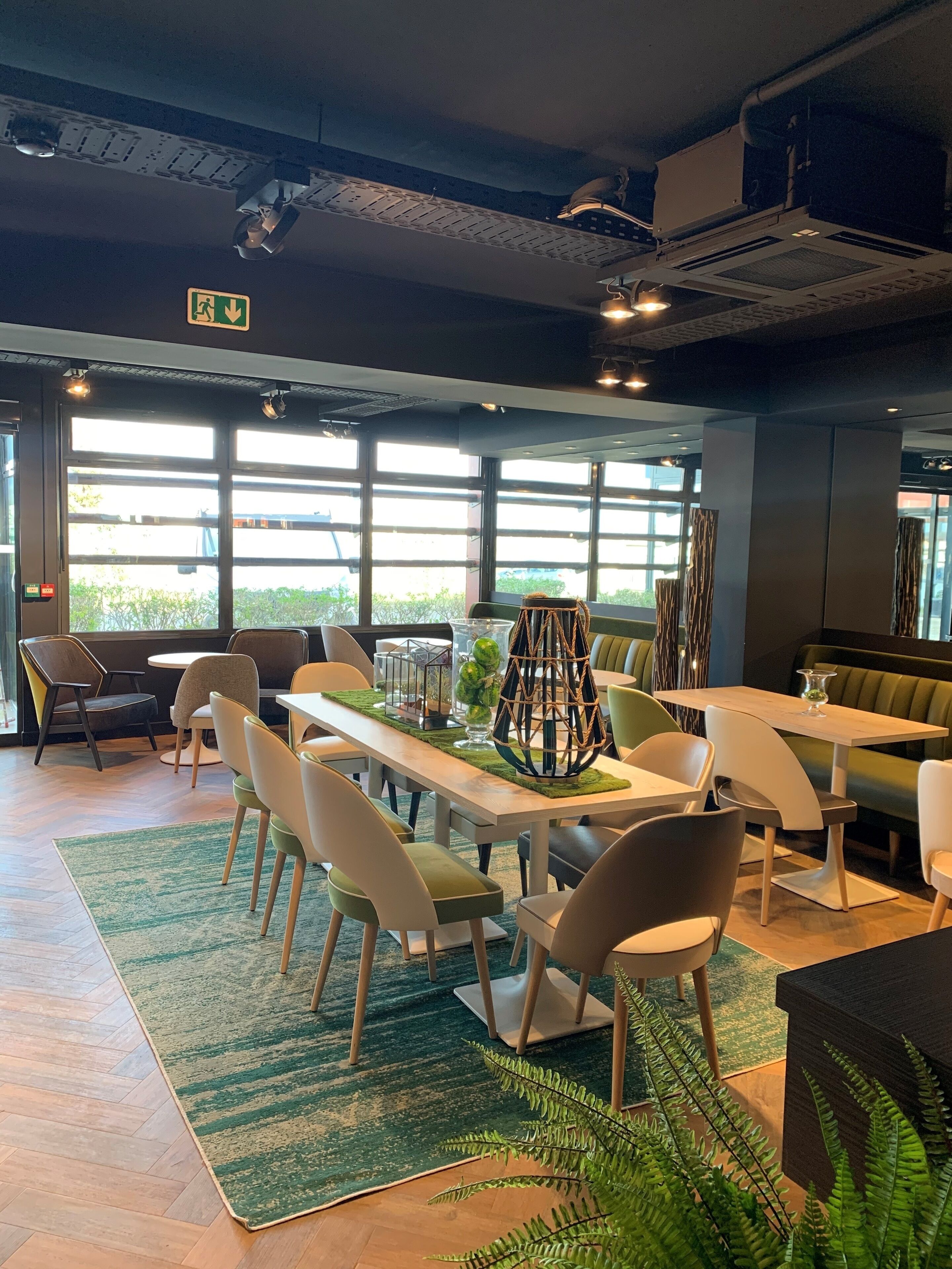 Um restaurante moderno com uma mesa de jantar comprida, várias cadeiras e vista através de grandes janelas.