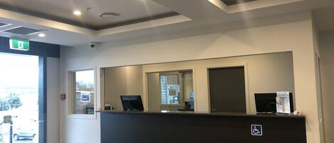 Uma receção com computador, sinal de acessibilidade para cadeira de rodas e vista para o exterior.