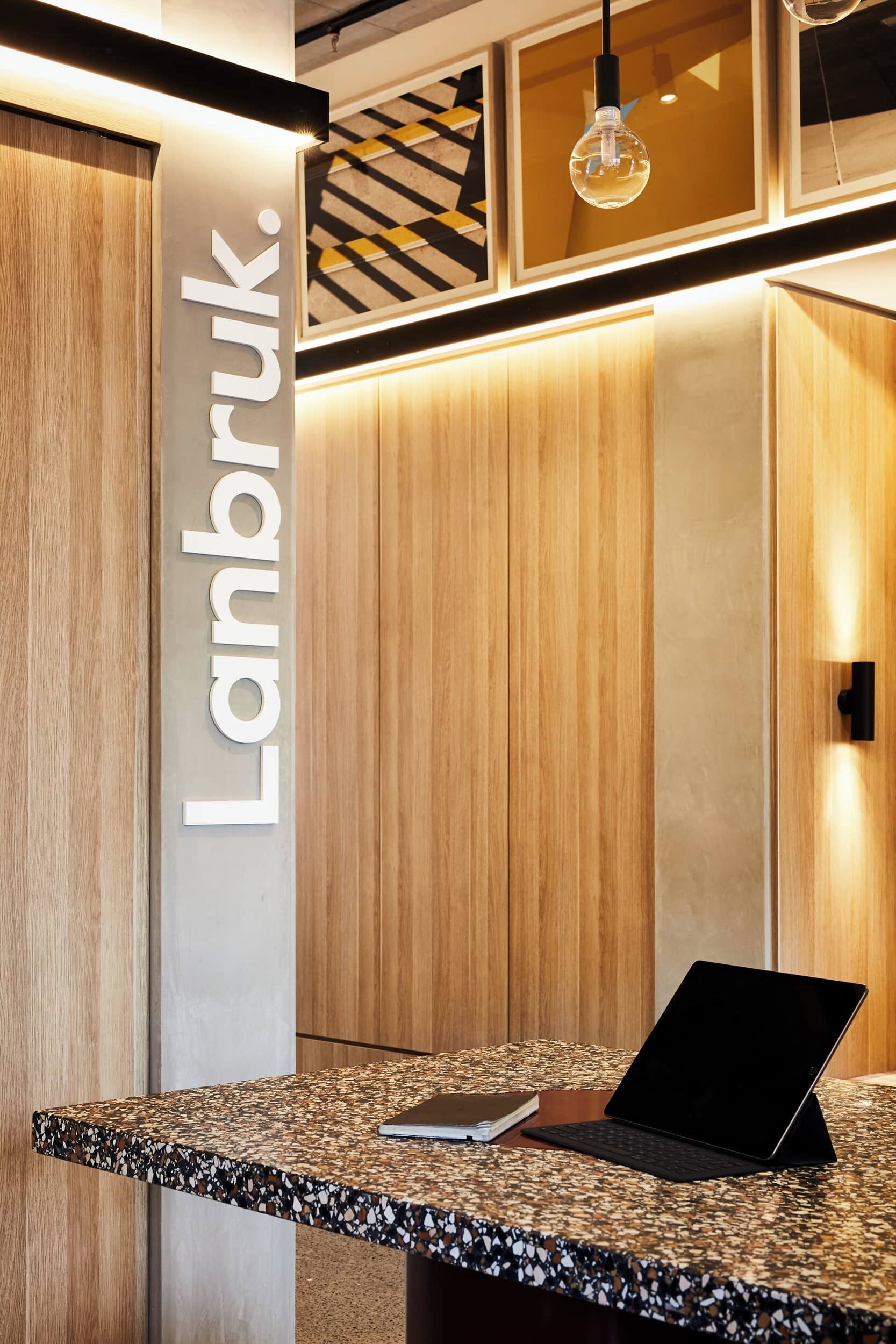 Uma receção com um computador portátil, um letreiro com a inscrição 'Lanbruk' e um design de interiores moderno.
