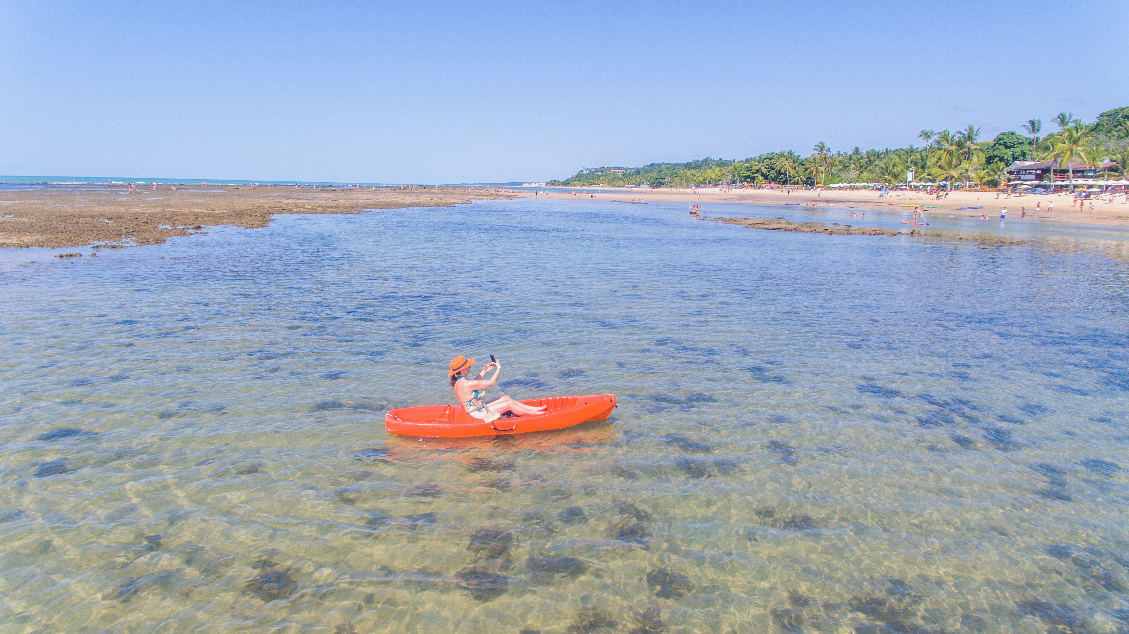 Visão nítida de uma praia com uma pessoa praticando caiaque na água.
