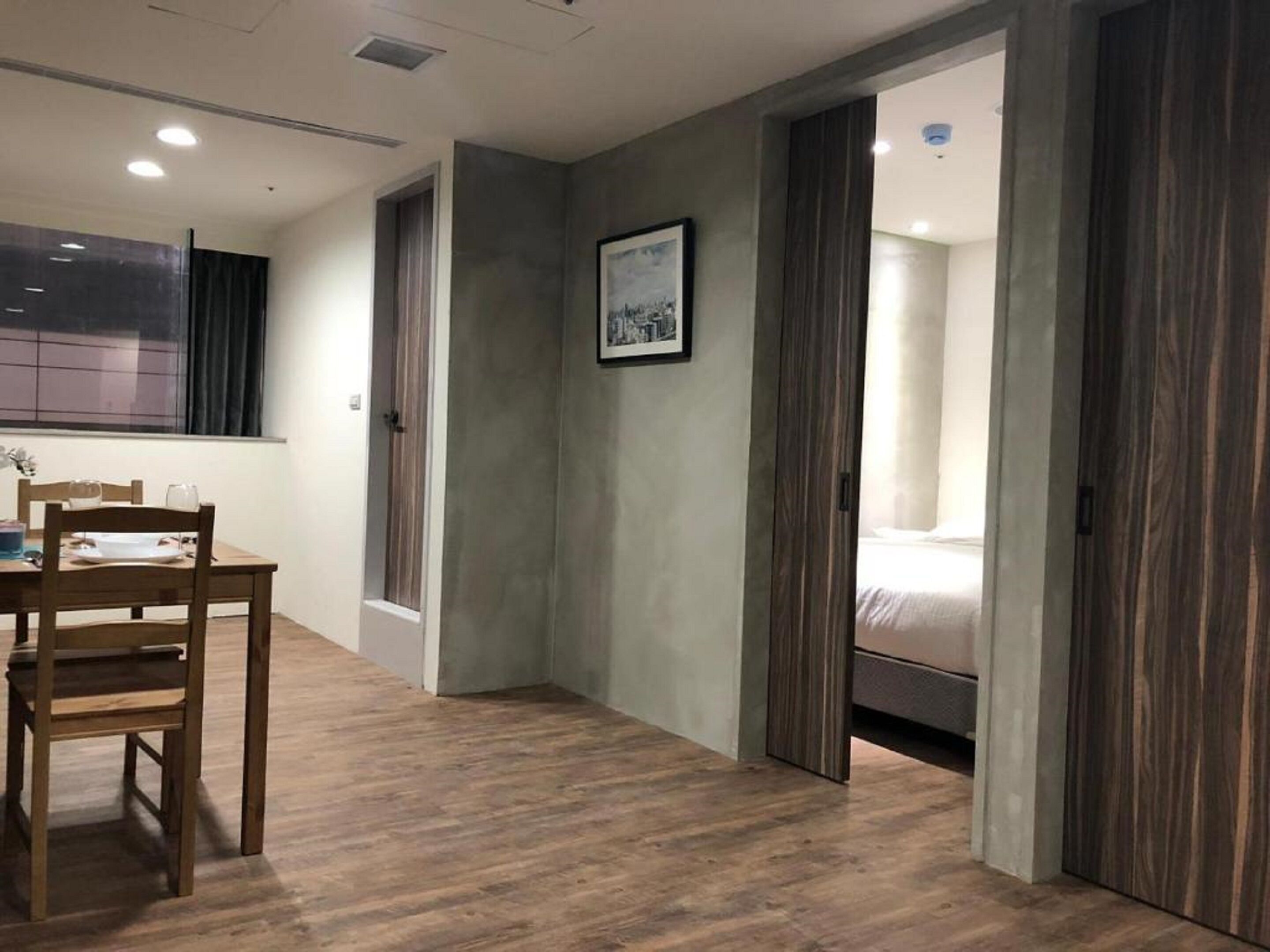 Quarto de hotel com piso de madeira, cama, mesa de cabeceira e uma janela.