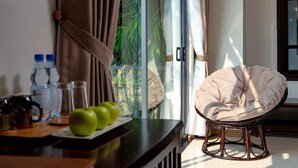 Quarto com uma mesa de jantar, garrafas de água, copos e maçãs. Há uma cadeira com almofada e uma janela com cortinas.
