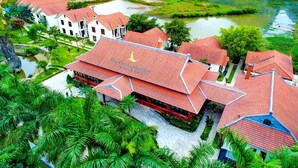 Um edifício tradicional com telhados de telha vermelha, rodeado por vegetação exuberante e um rio.